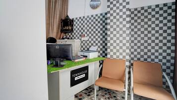 Uma área de recepção com parede xadrez, um relógio, uma mesa com computador e uma cadeira.