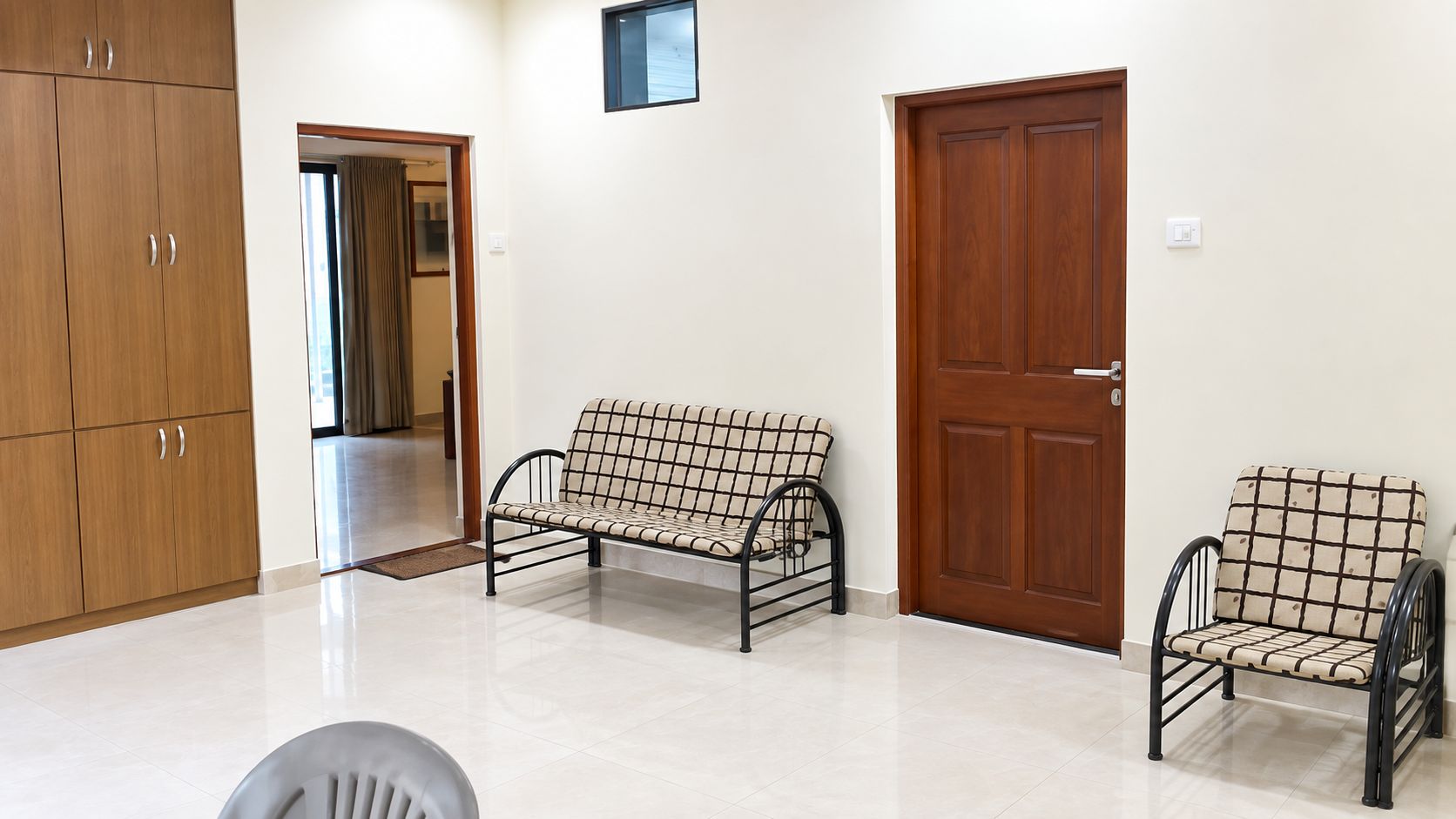 Quarto com sofá, cadeira, guarda-roupa de madeira e uma porta.