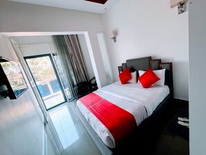 Quarto de hotel com cama, mesa de cabeceira, escrivaninha e vista para o exterior.