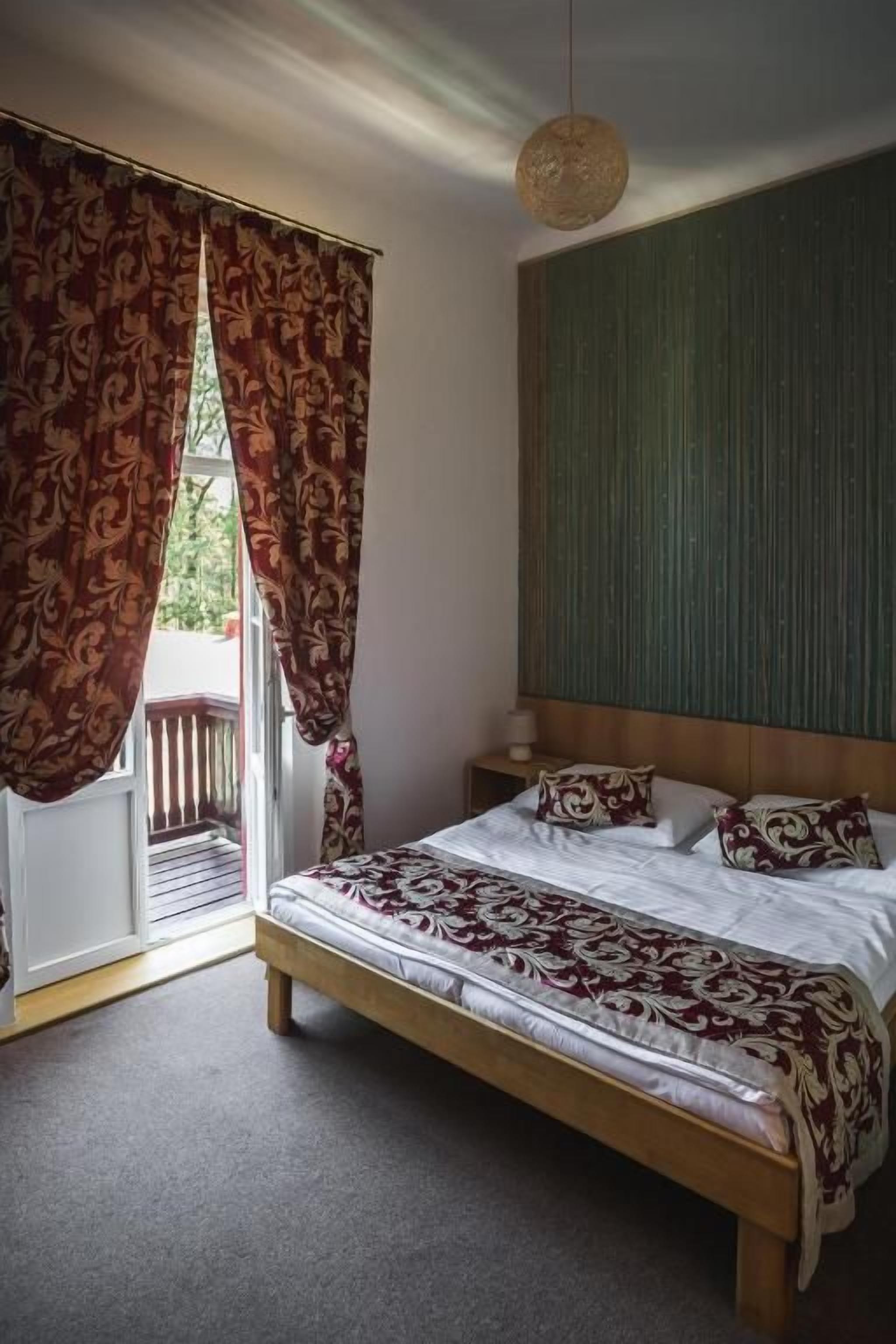 Quarto com cama, cortinas, luminária pendente e vista pela janela.