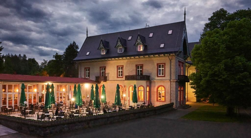 Um edifício grande com várias janelas e uma varanda, rodeado por um muro de pedra e vegetação.