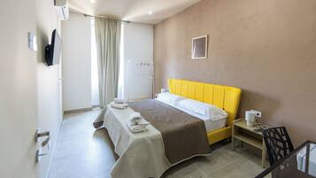Quarto de hotel com cama, mesa de cabeceira, cadeira, janela com cortinas e ar condicionado fixado na parede.