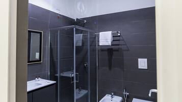 Um banheiro moderno com chuveiro em cabine de vidro, um bidê e um vaso sanitário.