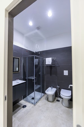 Um banheiro moderno com chuveiro em cabine de vidro, um bidê e um vaso sanitário.