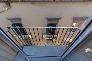 Vista de uma varanda com guarda-corrimão de metal, mostrando um edifício com várias janelas e persianas.