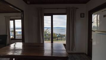 Quarto com mesa de madeira, vista para um corpo d'água e porta que dá para o exterior.