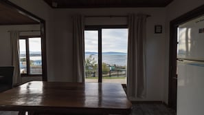 Quarto com mesa de madeira, vista para um corpo d'água e porta que dá para o exterior.