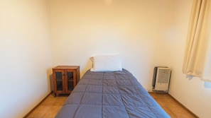 Quarto pequeno e estreito com uma cama, um armário de madeira e um aquecedor.
