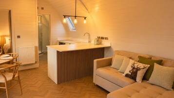 Um interior acolhedor com piso de madeira, um sofá com almofadas estampadas, uma área de jantar com mesa e cadeiras, e uma cozinha com ilha central.