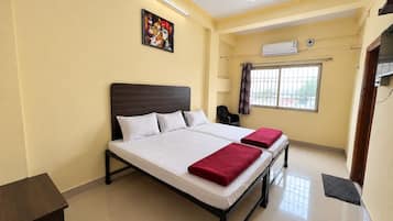 Quarto de hotel com cama, escrivaninha, ventoinha no teto, ar condicionado e janela com cortinas.