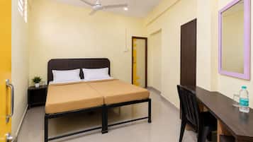 Quarto de hotel com cama, escrivaninha, cadeira, ventoinha de teto e espelho.