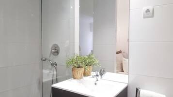 Casa de banho moderna com chuveiro em cabine de vidro, lavatório branco e duas plantas em vasos.