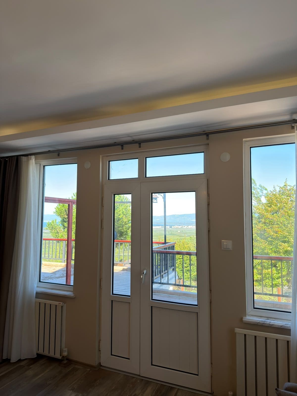 Quarto com uma grande porta de vidro deslizante que dá para uma varanda com vista para áreas verdes e uma paisagem distante.