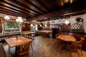 Interior de restaurante com mesas e bancos de madeira, luminárias pendentes e vista para o exterior.