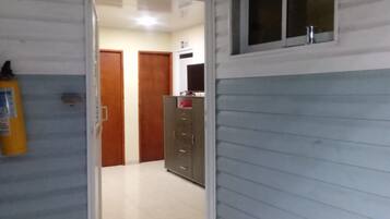 Um corredor com uma porta que dá para um quarto, um extintor de incêndio e uma janela com vista.