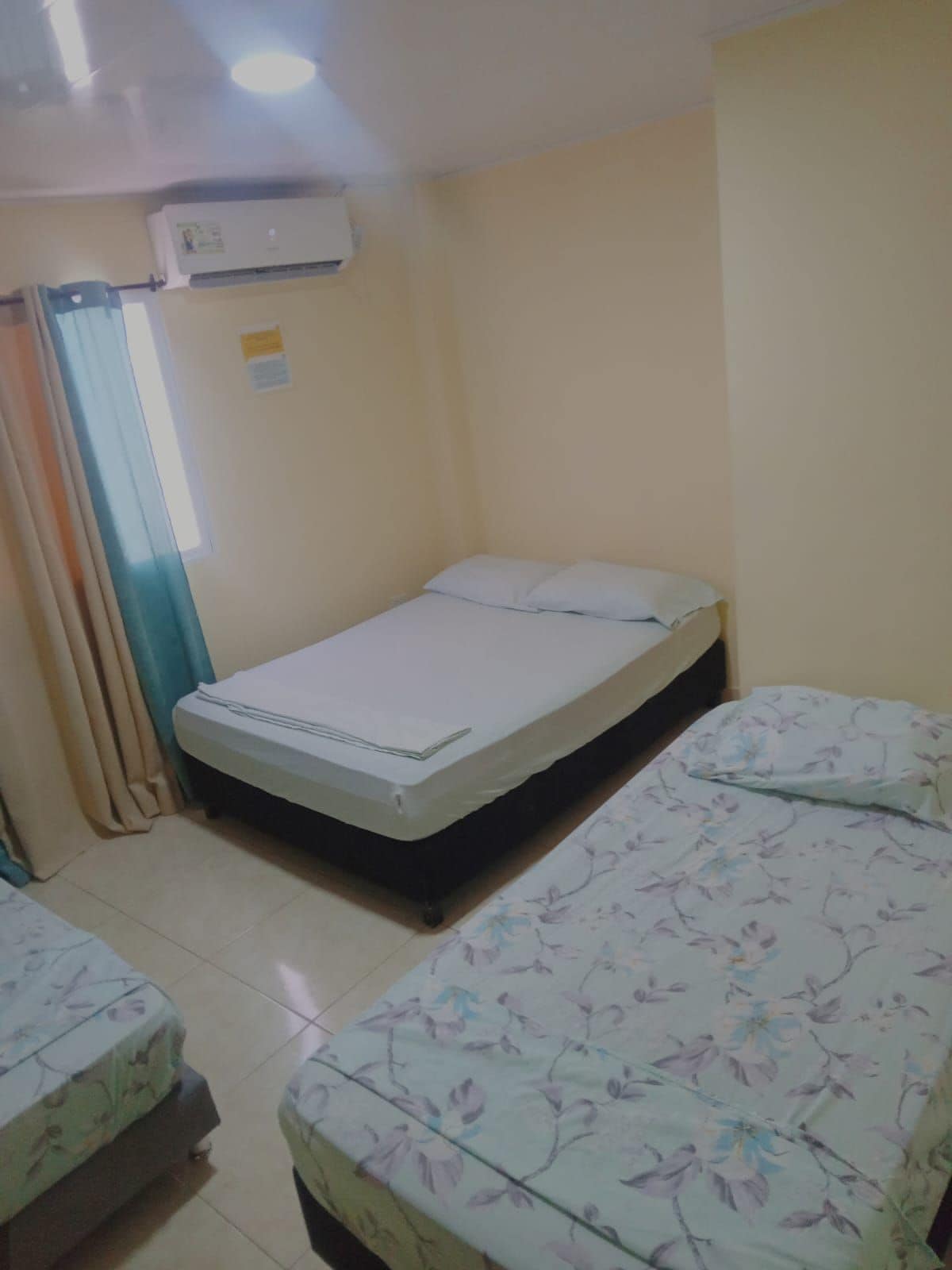 Quarto com uma cama de solteiro, outra cama e janela com cortinas.