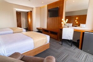 Quarto de hotel com duas camas, uma escrivaninha, televisão e um espelho.