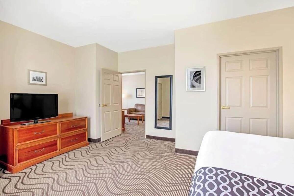 Quarto de hotel com cama, televisão, penteadeira, espelho e porta.