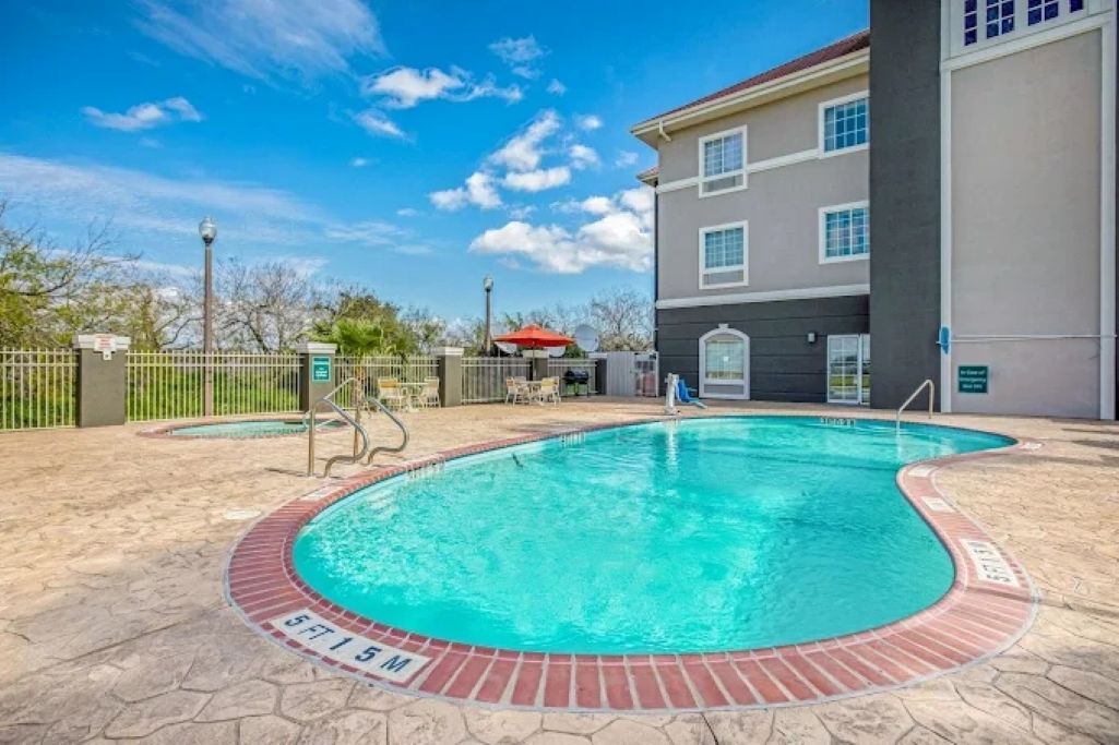Piscina com borda de tijolos, área de estar coberta e um edifício com fachada cinzenta.