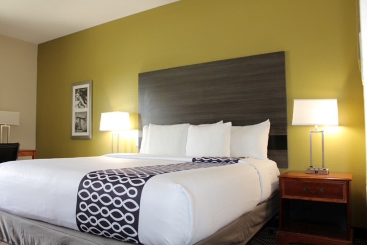 Quarto de hotel com uma cama grande, duas luminárias de cabeceira, uma mesa de apoio e um quadro na parede.