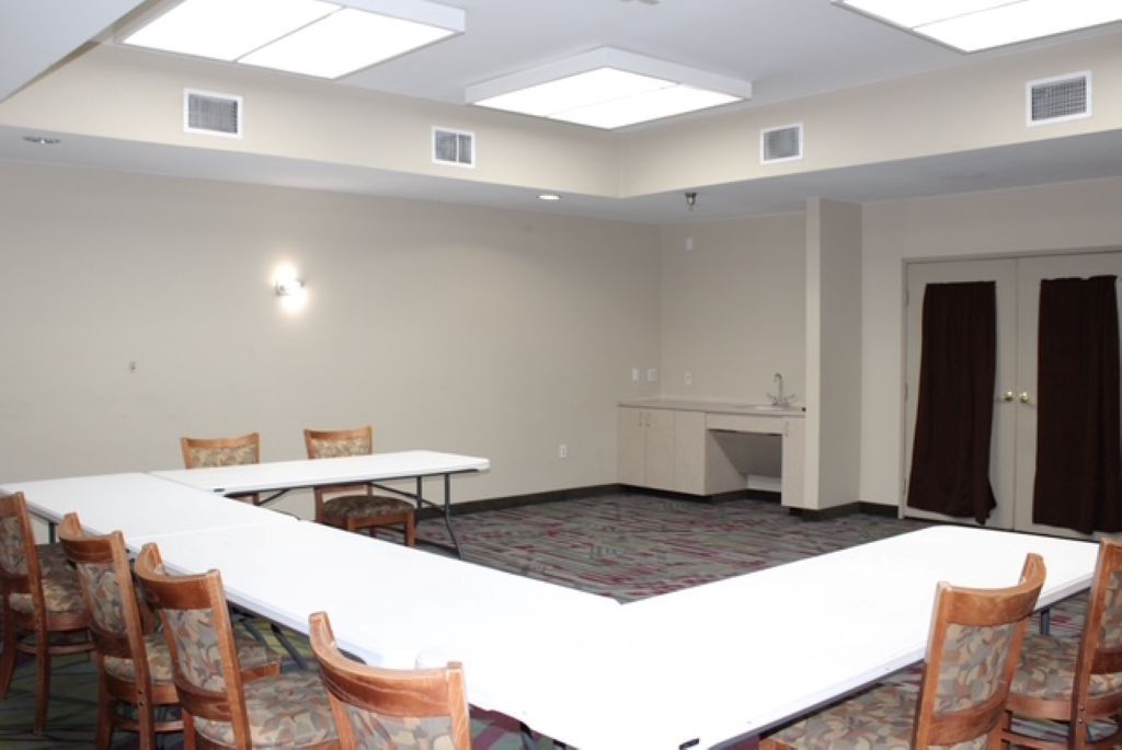 Uma sala de conferências com uma mesa comprida e cadeiras, uma copa e uma porta com cortinas.
