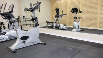 Academia com bicicletas ergométricas, esteira e espelho refletindo os equipamentos.