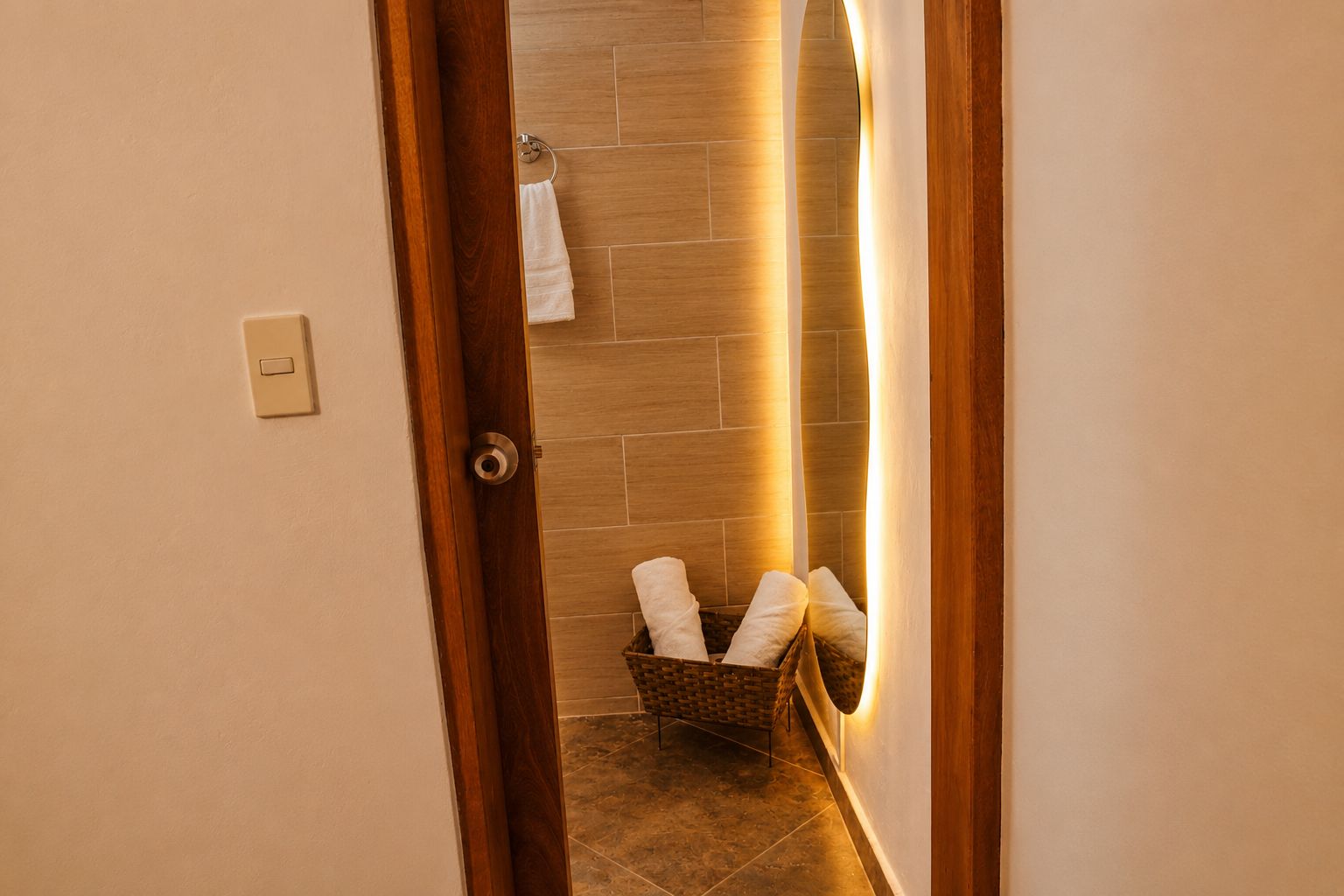 Corredor que leva a um banheiro, com porta de madeira, porta-toalhas e um cesto com toalhas.