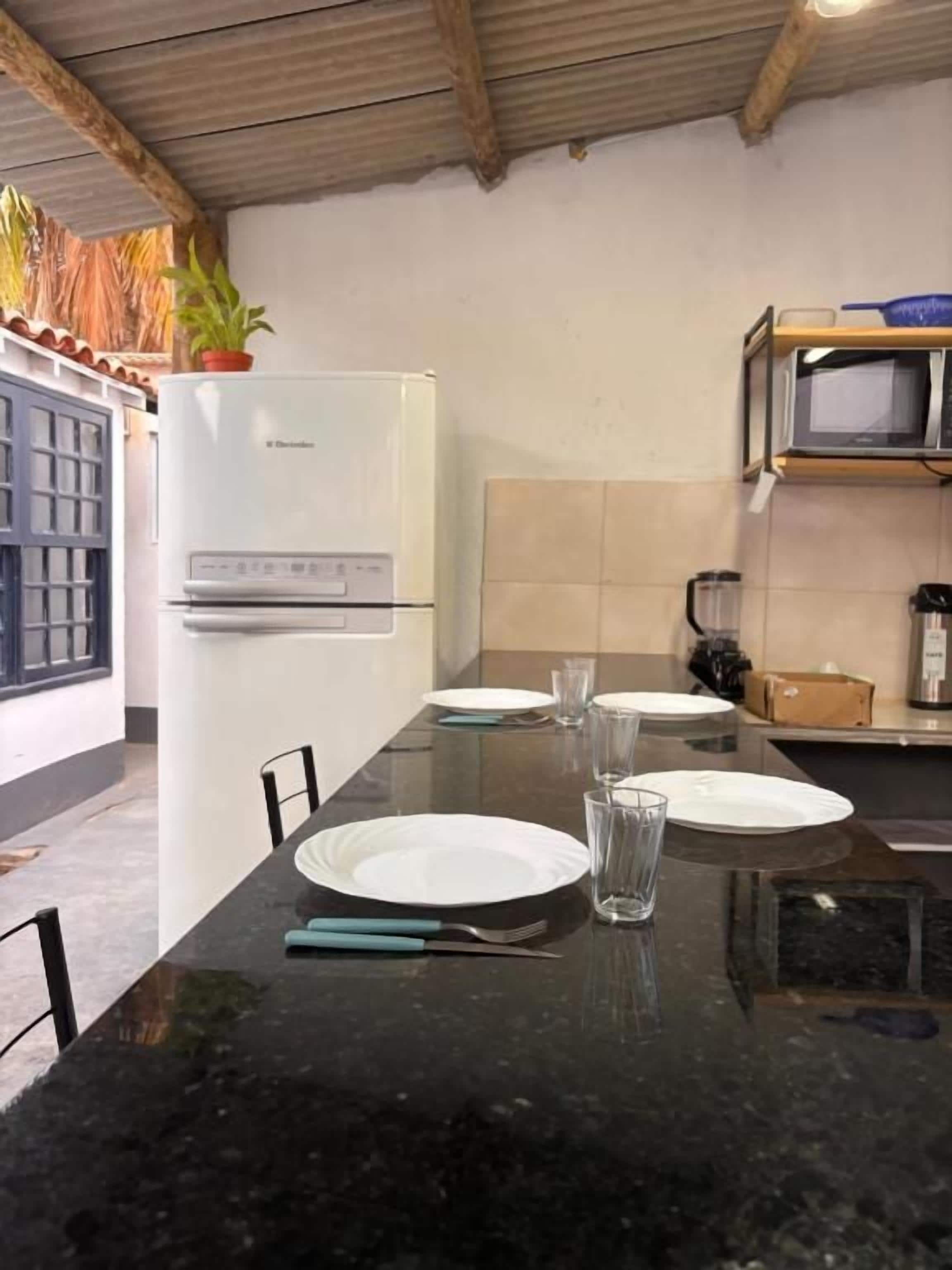 Cozinha com bancada preta, pratos brancos e geladeira.