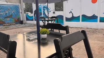 Um pátio externo com mesa, cadeiras, guarda-sóis e um mural na parede.