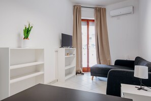 Sala de estar minimalista com televisão de tela plana, sofá, mesinha e um vaso de planta.
