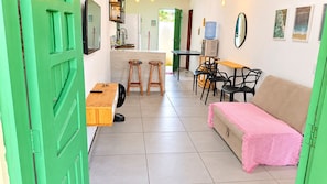 Um quarto com porta verde, um sofá com manta rosa, uma mesa de madeira e uma cadeira.