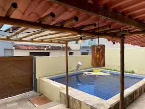 Piscina no terraço com pergolado de madeira, cercada por um muro baixo e um portão de metal.