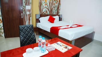 Quarto de hotel com uma cama, uma mesa vermelha, uma cadeira e uma parede com padrão de árvore.