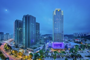 Paisagem urbana com dois edifícios altos e imponentes, área de estacionamento e um prédio comercial bem iluminado.