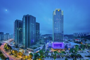 Paisagem urbana com dois edifícios altos e imponentes, área de estacionamento e um prédio comercial bem iluminado.