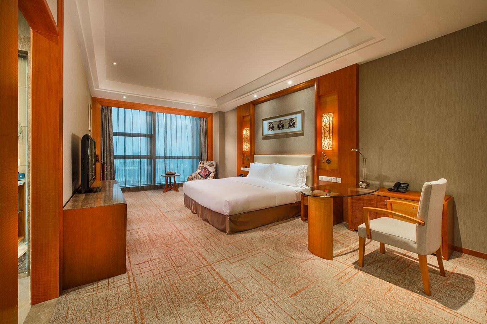 Quarto de hotel com uma cama grande, uma escrivaninha com cadeira, televisão e uma janela com cortinas.