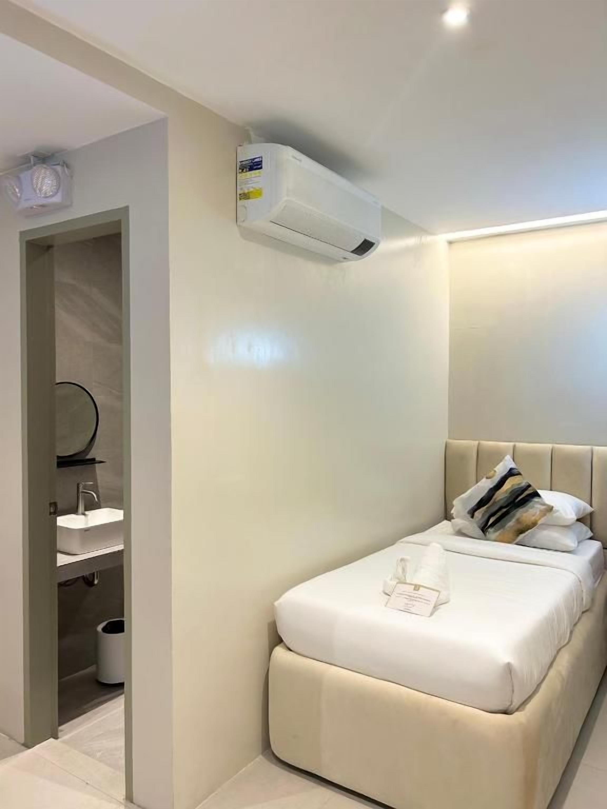 Quarto de hotel moderno com cama, penteadeira embutida e unidade de ar condicionado no teto.