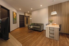 Uma sala de estar moderna com sofá, mesa de centro e televisão. O chão é de madeira, há um candeeiro de parede e uma porta com espelho.