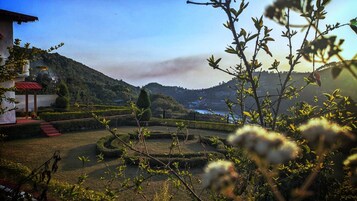 Um jardim bem cuidado com um gazebo, gramado impecável e vista para uma colina distante.