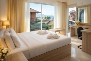 Quarto de hotel com cama, escrivaninha, cadeira, luminária e vista para o exterior.