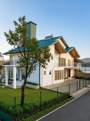 Uma casa moderna de dois andares com telhado verde, varanda visível e gramado bem cuidado.