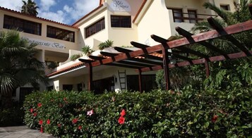 Hotel com área externa coberta, um edifício com placa e vegetação exuberante.