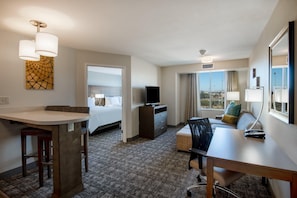 Quarto de hotel com escrivaninha, cadeira, televisão e sofá com vista para a cidade.