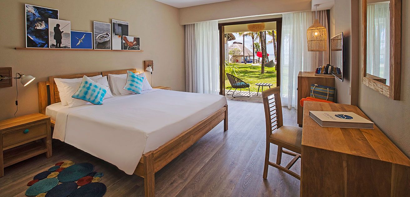 Quarto de hotel com uma cama grande, mobiliário de madeira, uma escrivaninha e vista para o exterior.