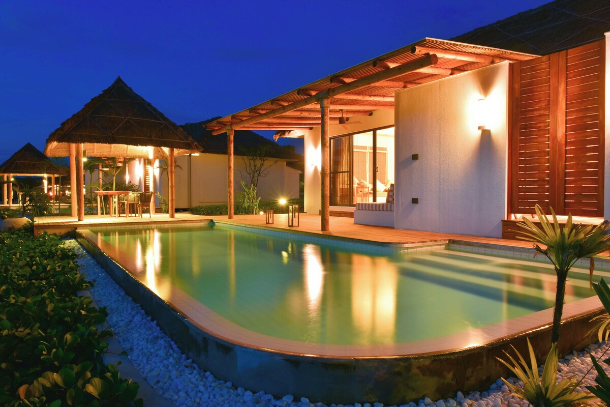 Um resort com piscina, área de estar coberta e estrutura com telhado de palha.