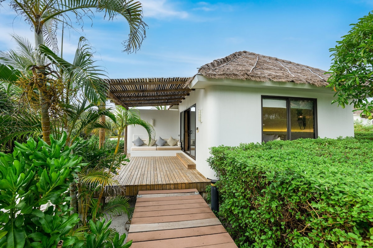 Uma casa moderna com deck de madeira, telhado de palha e vegetação exuberante.