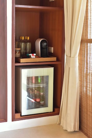 Minibar com cafeteira, garrafas e um refrigerador com bebidas.