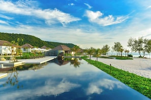 Resort com uma extensa piscina refletora, praia e montanhas ao fundo.