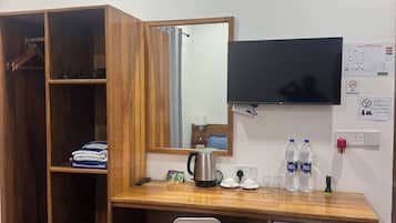 Quarto de hotel compacto com guarda-roupa de madeira, pequena escrivaninha com televisão, frigorífico e lixeira.
