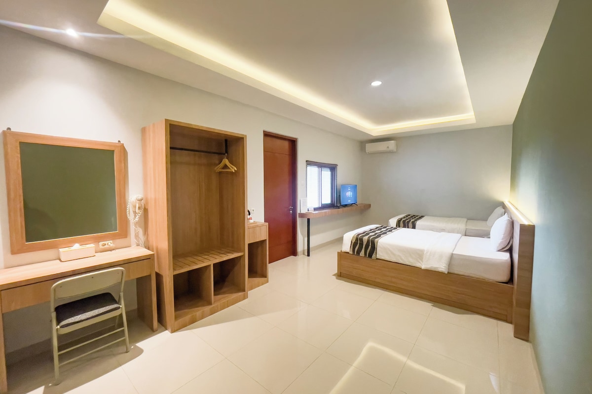Quarto de hotel com escrivaninha, cama, guarda-roupa e televisão.